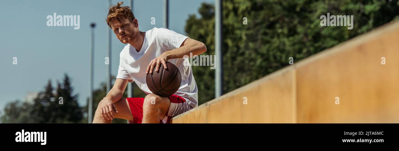 redhead basketball player sitting on stadium with ball, banner Stock ...
