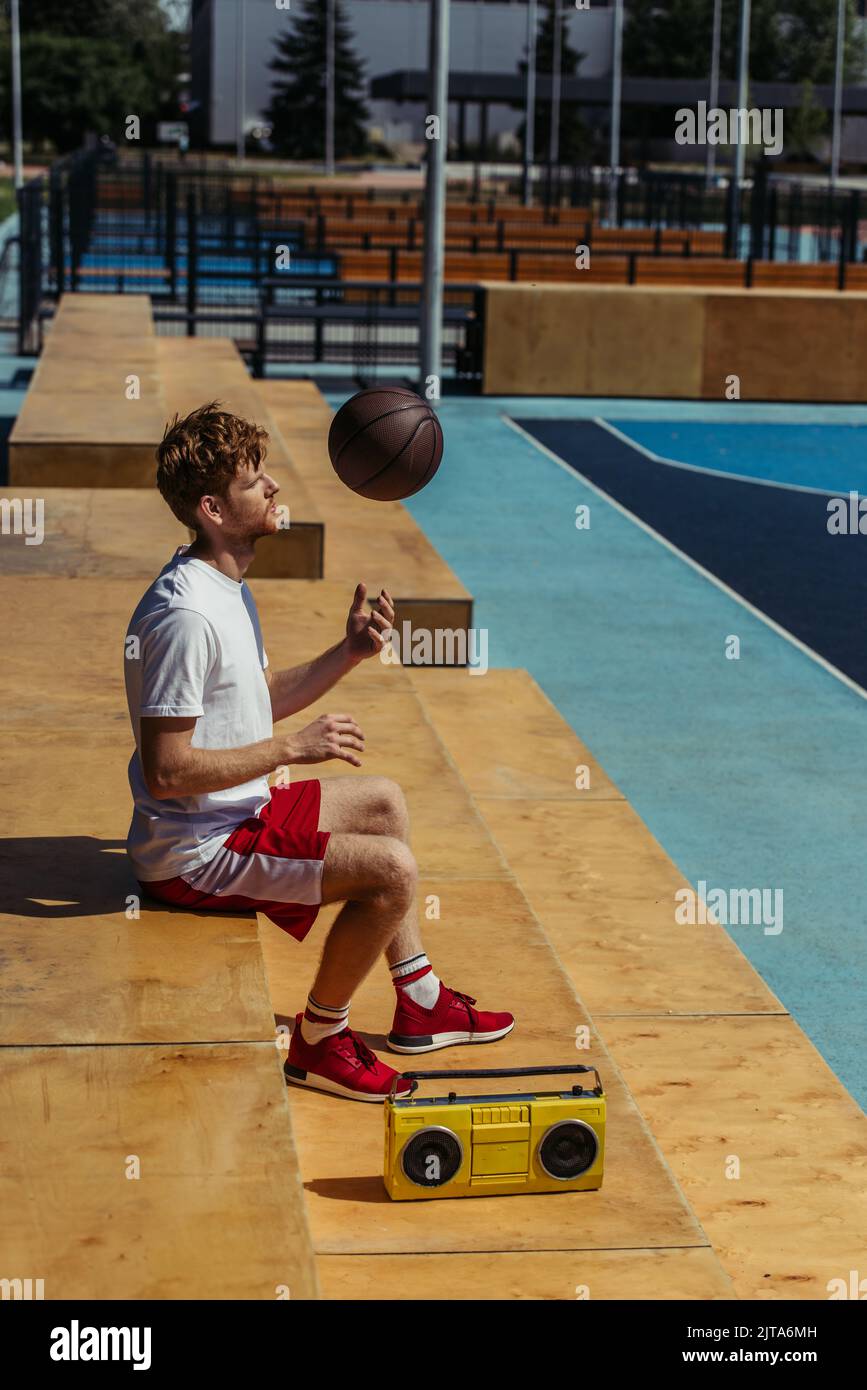 side view of sportive man playing with ball while sitting on stadium ...