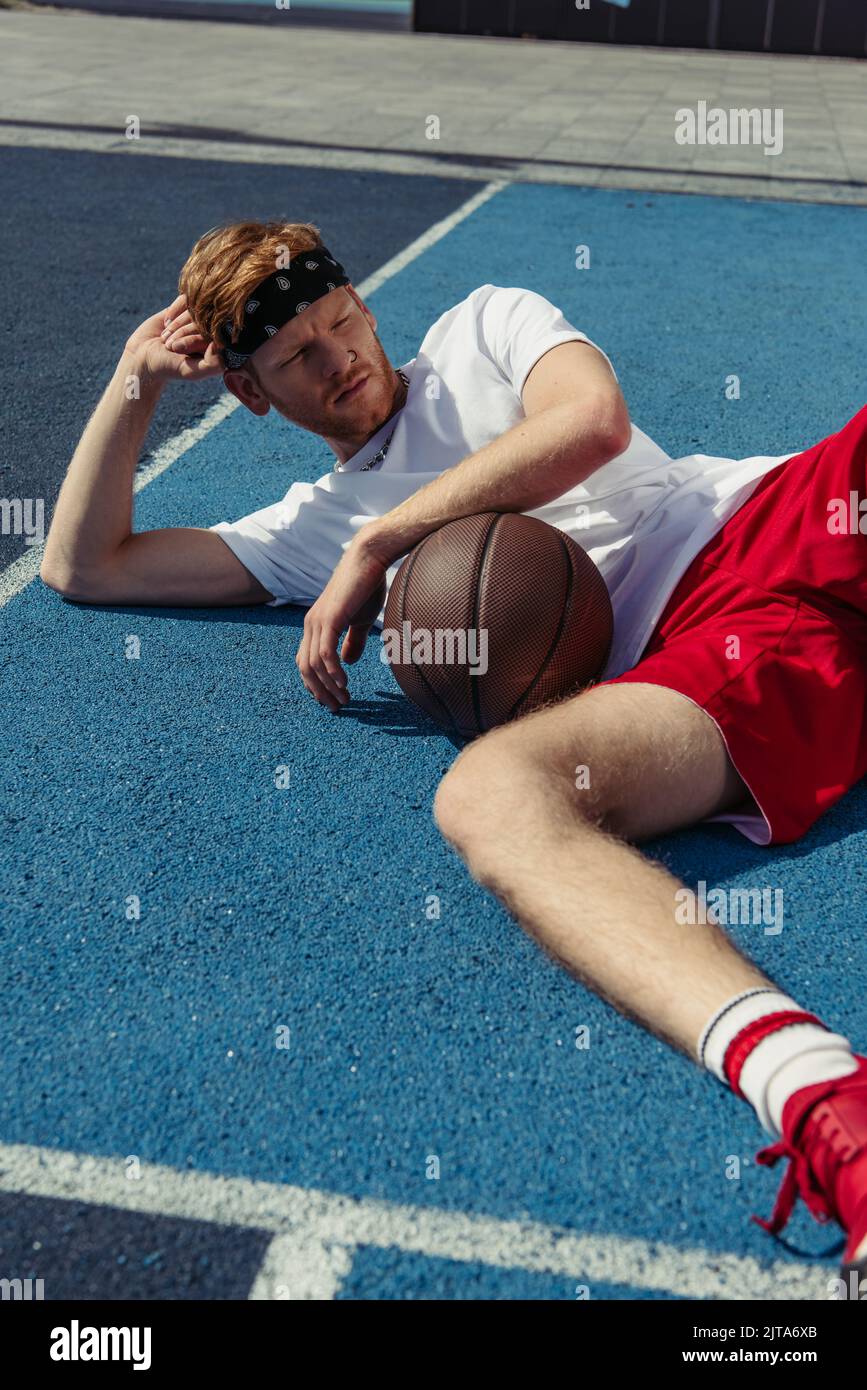 redhead basketball player in sportswear lying on court near ball and ...