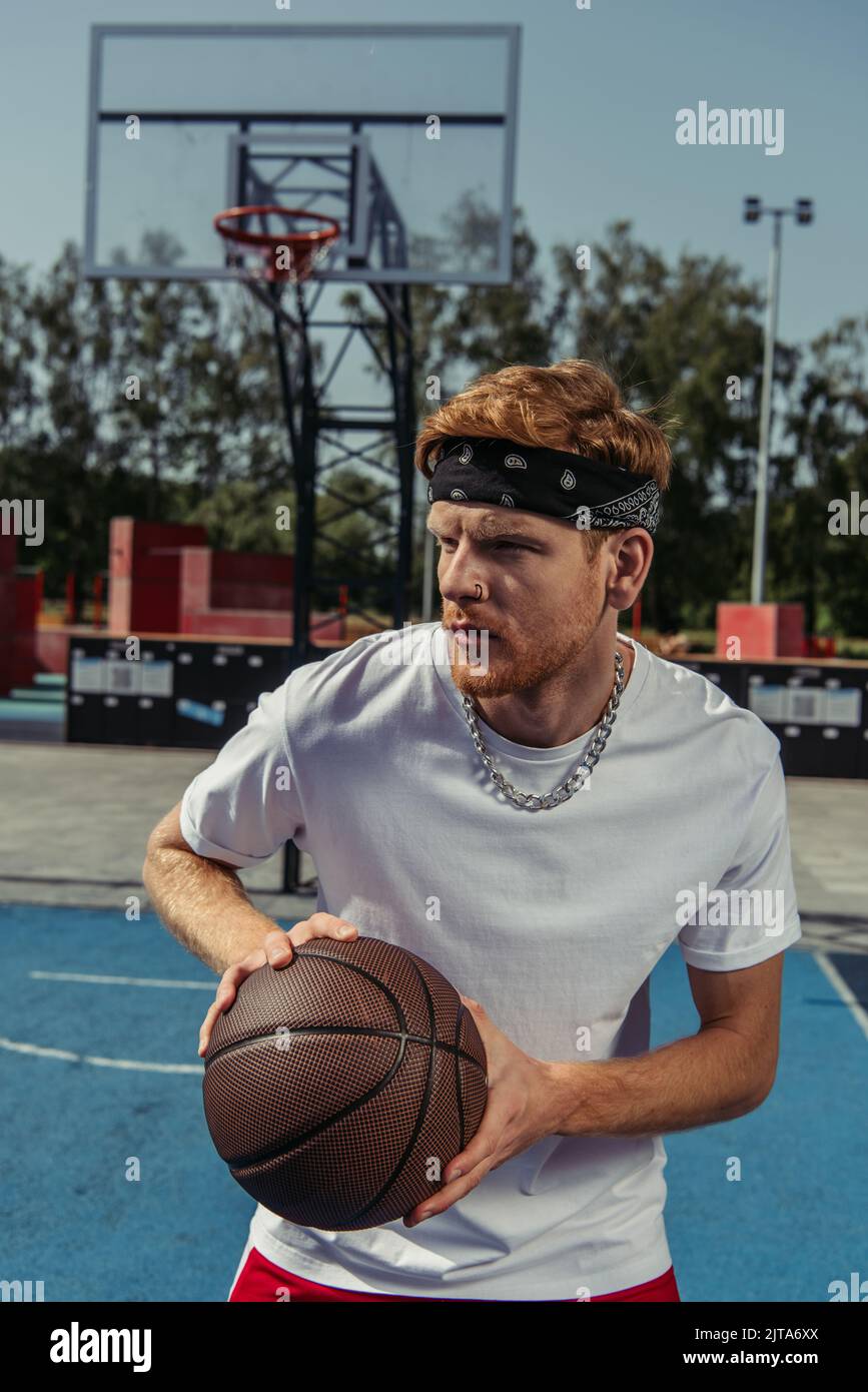 young sportsman in bandana and necklace playing basketball outdoors ...