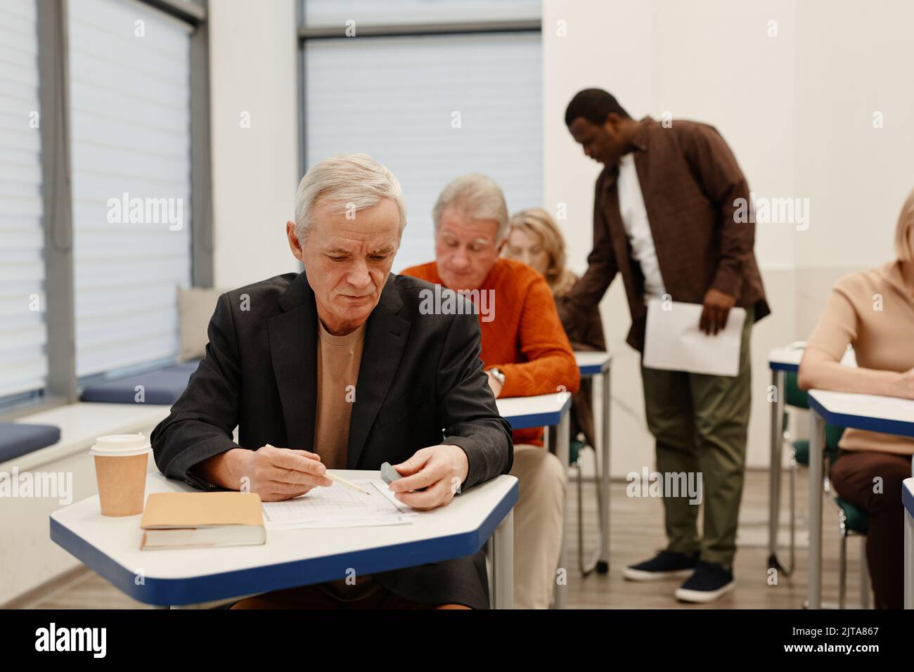 Senior students sitting at desks in a row and writing test during ...