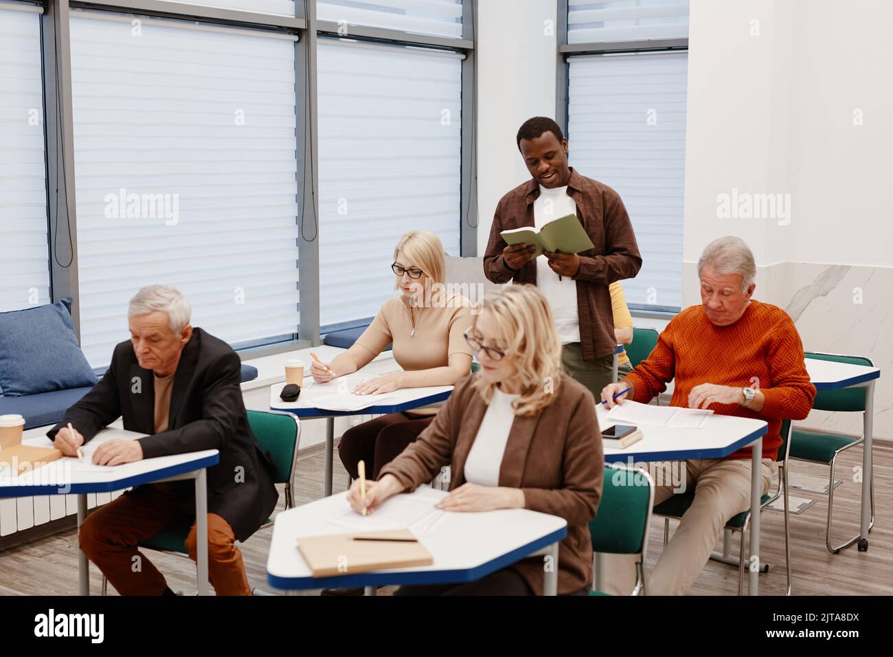 Group of senior students sitting at desks and making notes while ...