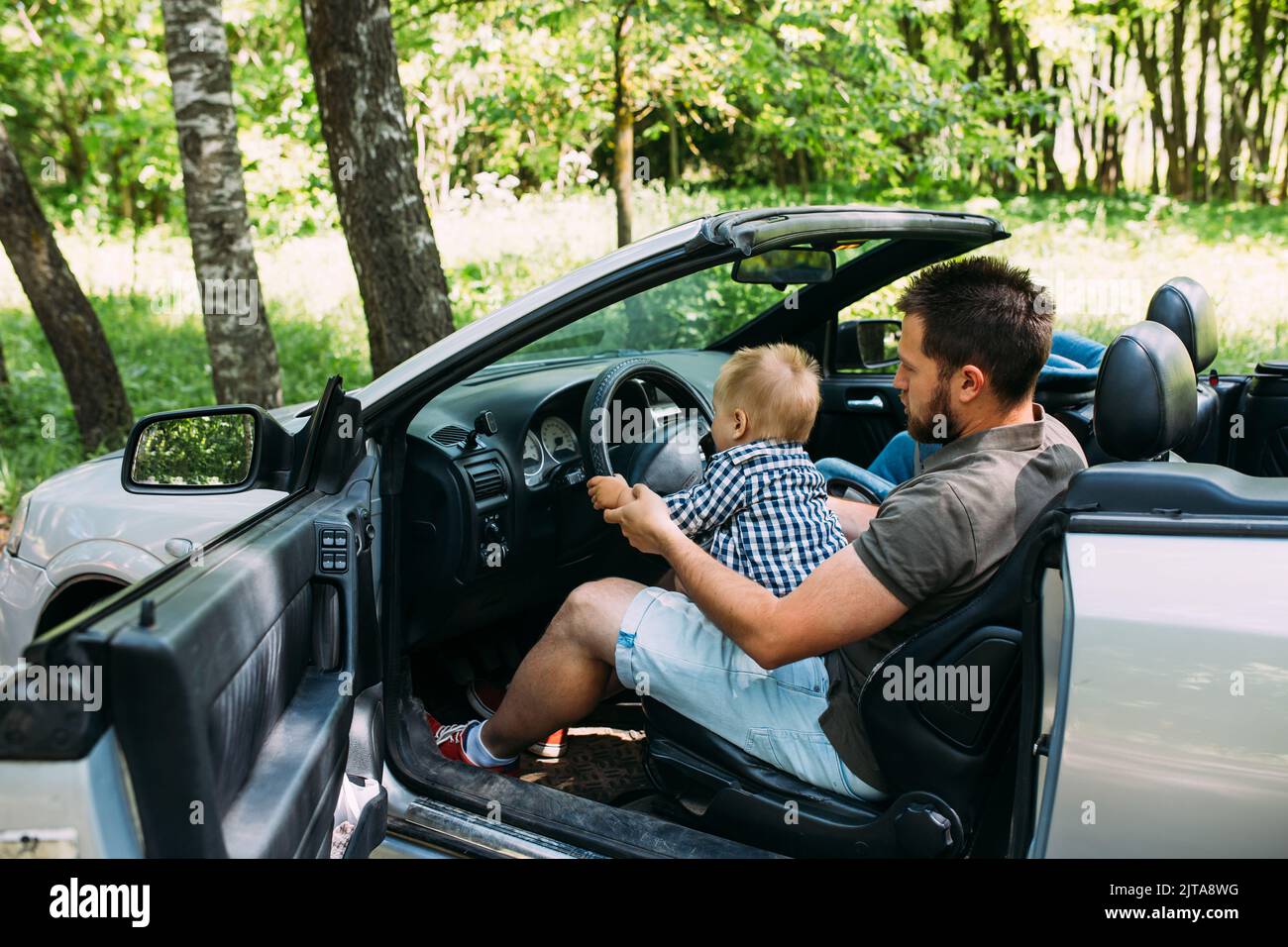 Dad shows his little son how to drive car while sitting behind wheel ...
