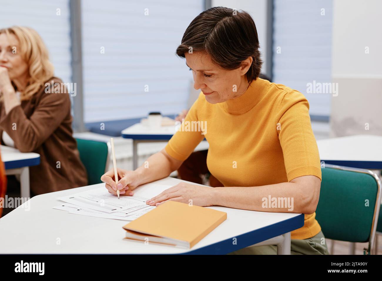 Mature woman with short hair making notes while sitting at desk during ...