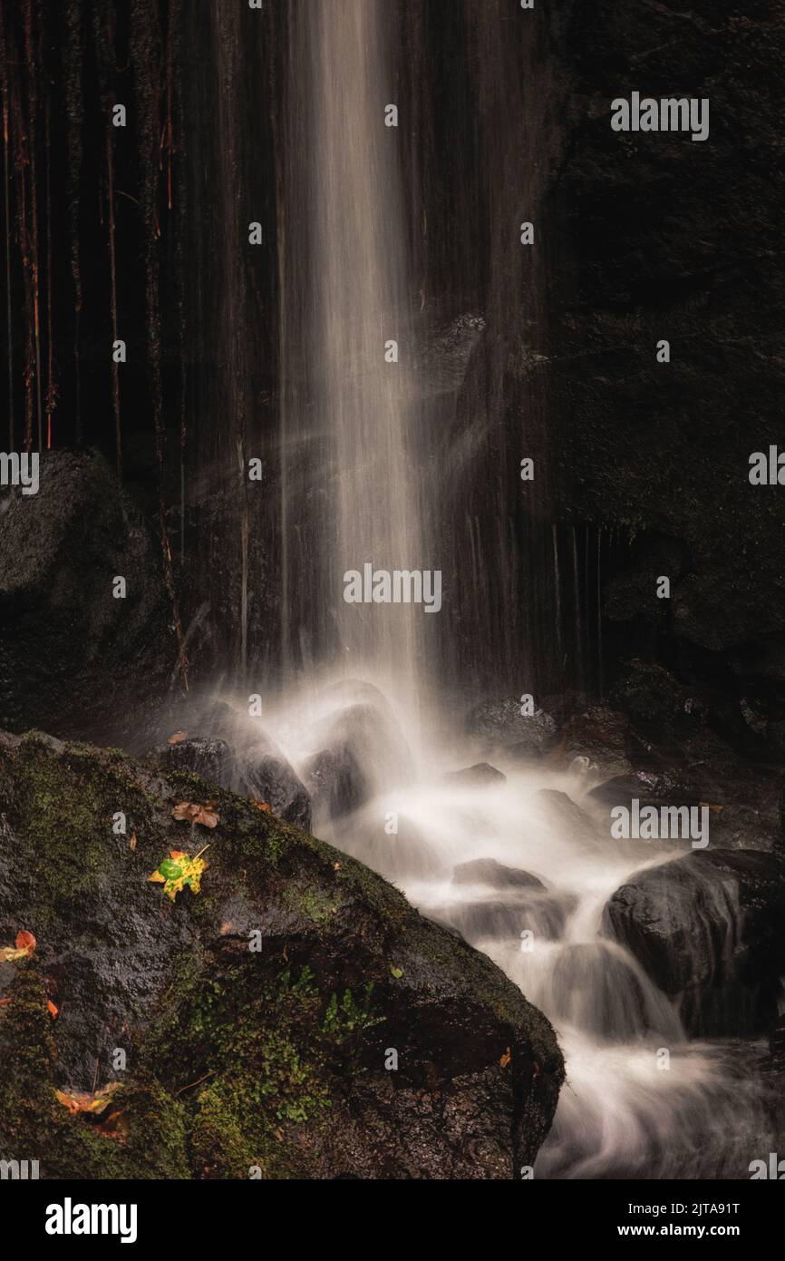 A vertical shot of a beautiful waterfall surrounded by dark rocks Stock ...