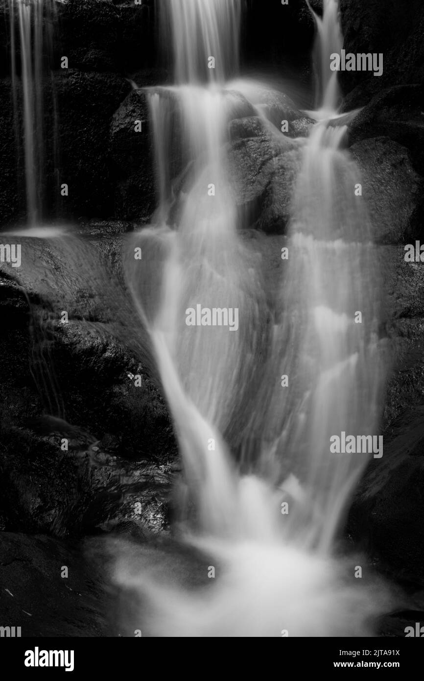 A vertical grayscale shot of a beautiful waterfall surrounded by rocks ...
