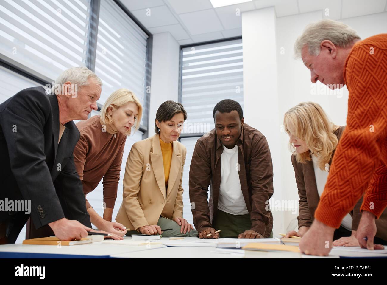 Group of senior students standing around the table and working in team ...
