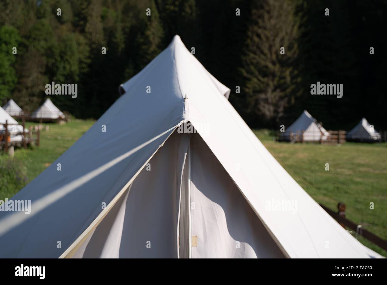 front view closeup of glamping tent top white fabric in green meadow ...