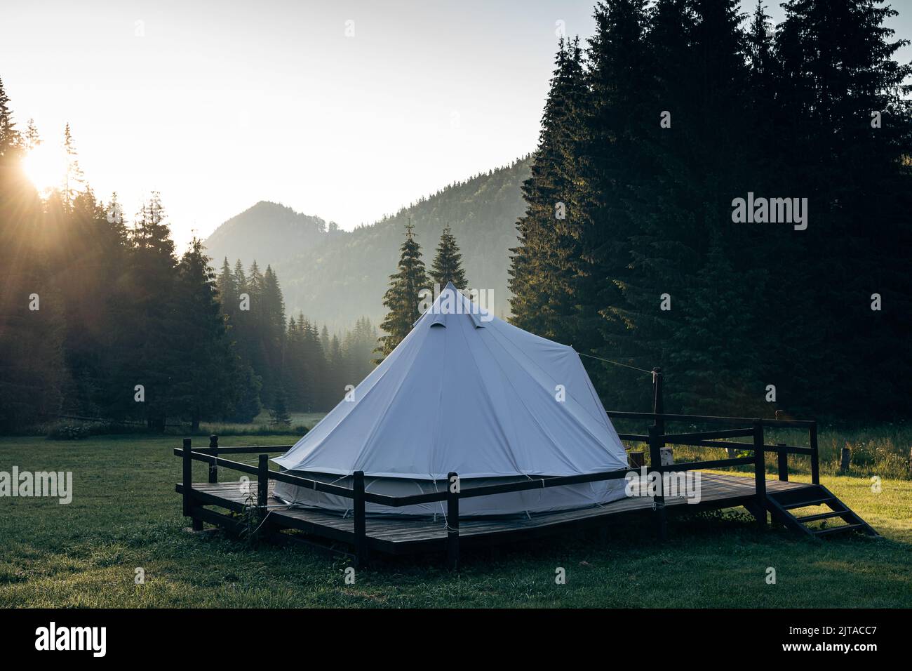 rear view of white glamping tent on wooden deck in green meadow ...