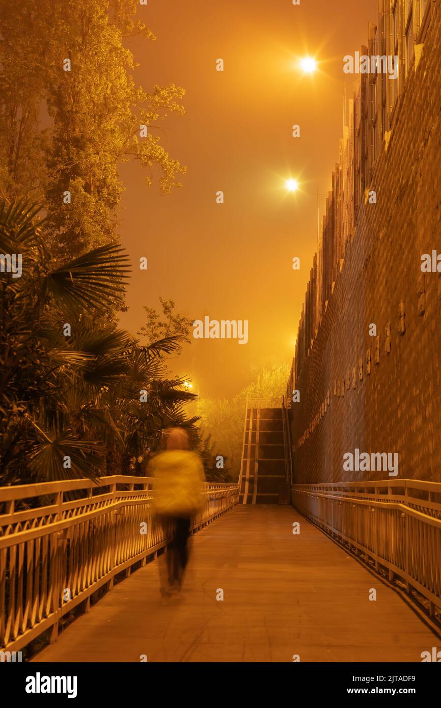 A blurred human figure runs along a night path leading into the fog ...