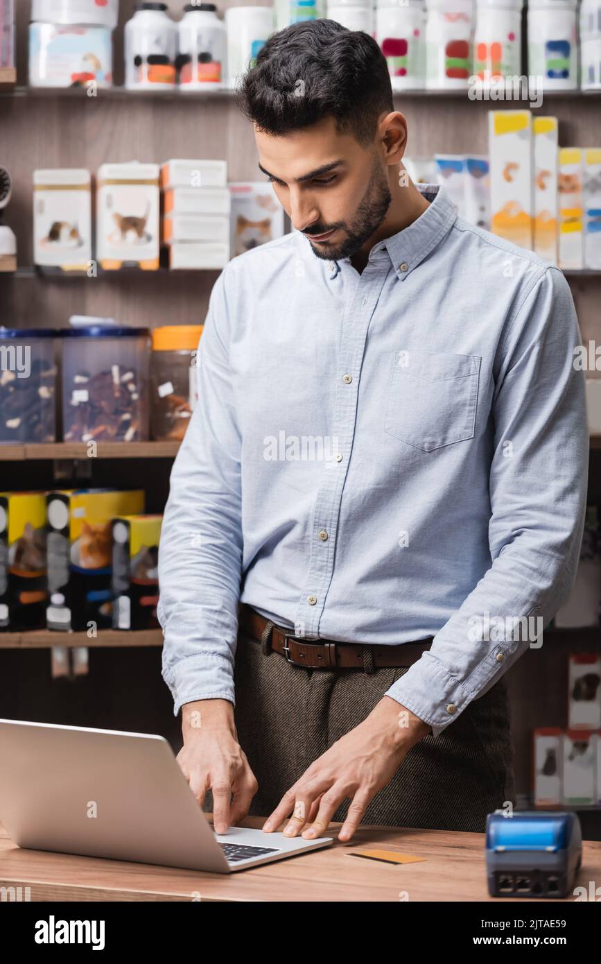 Arabian seller using laptop near payment terminal in pet shop Stock ...