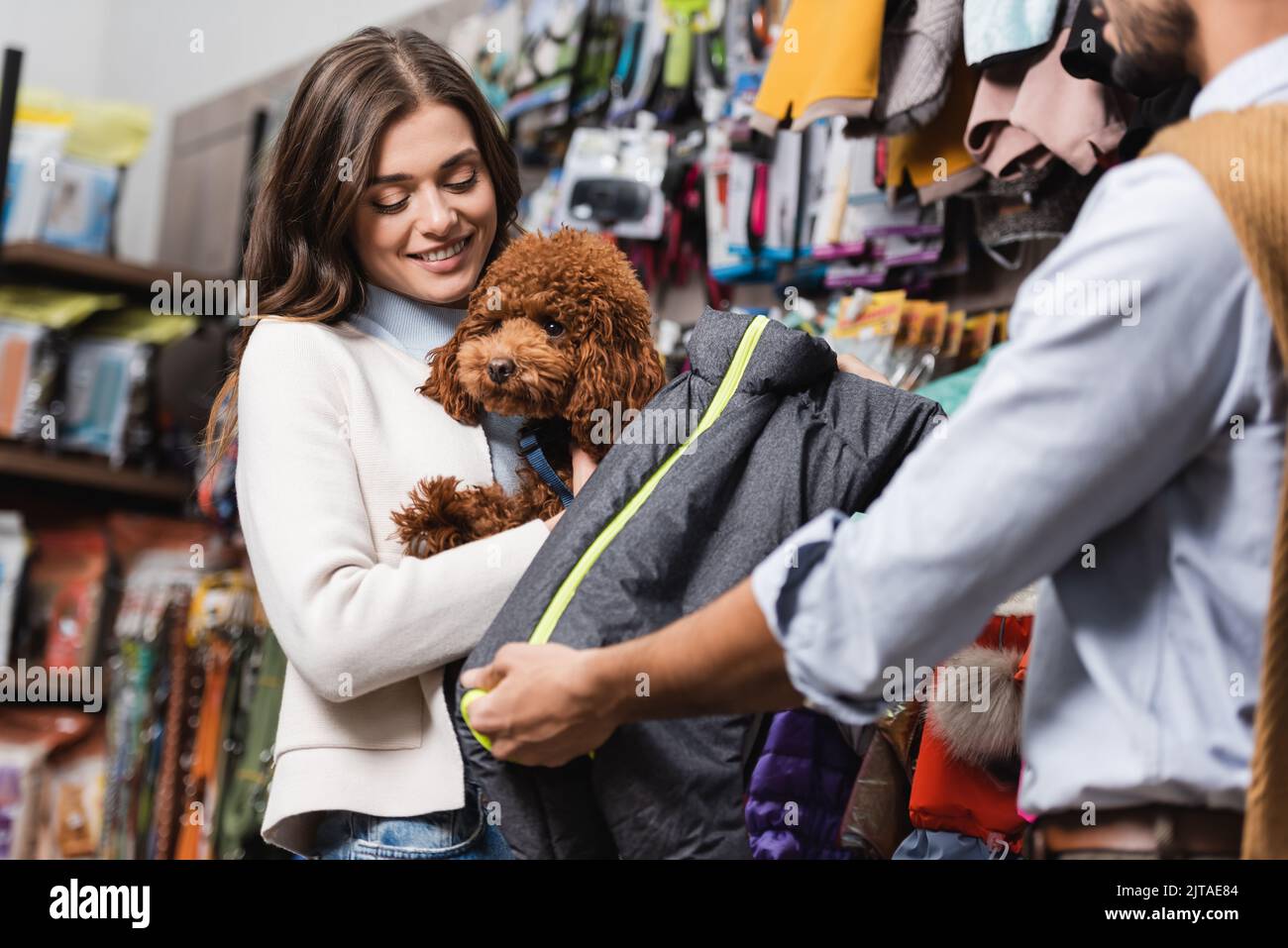 Cheerful woman holding brown poodle near boyfriend with animal jacket ...