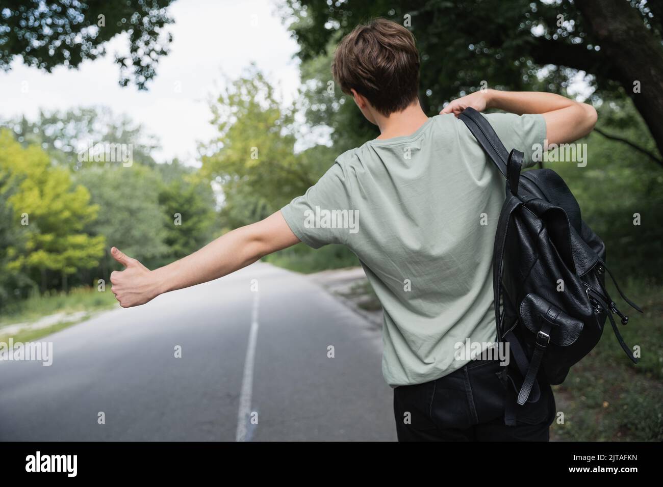 back view of hitchhiker with backpack stopping car with thumb up on ...