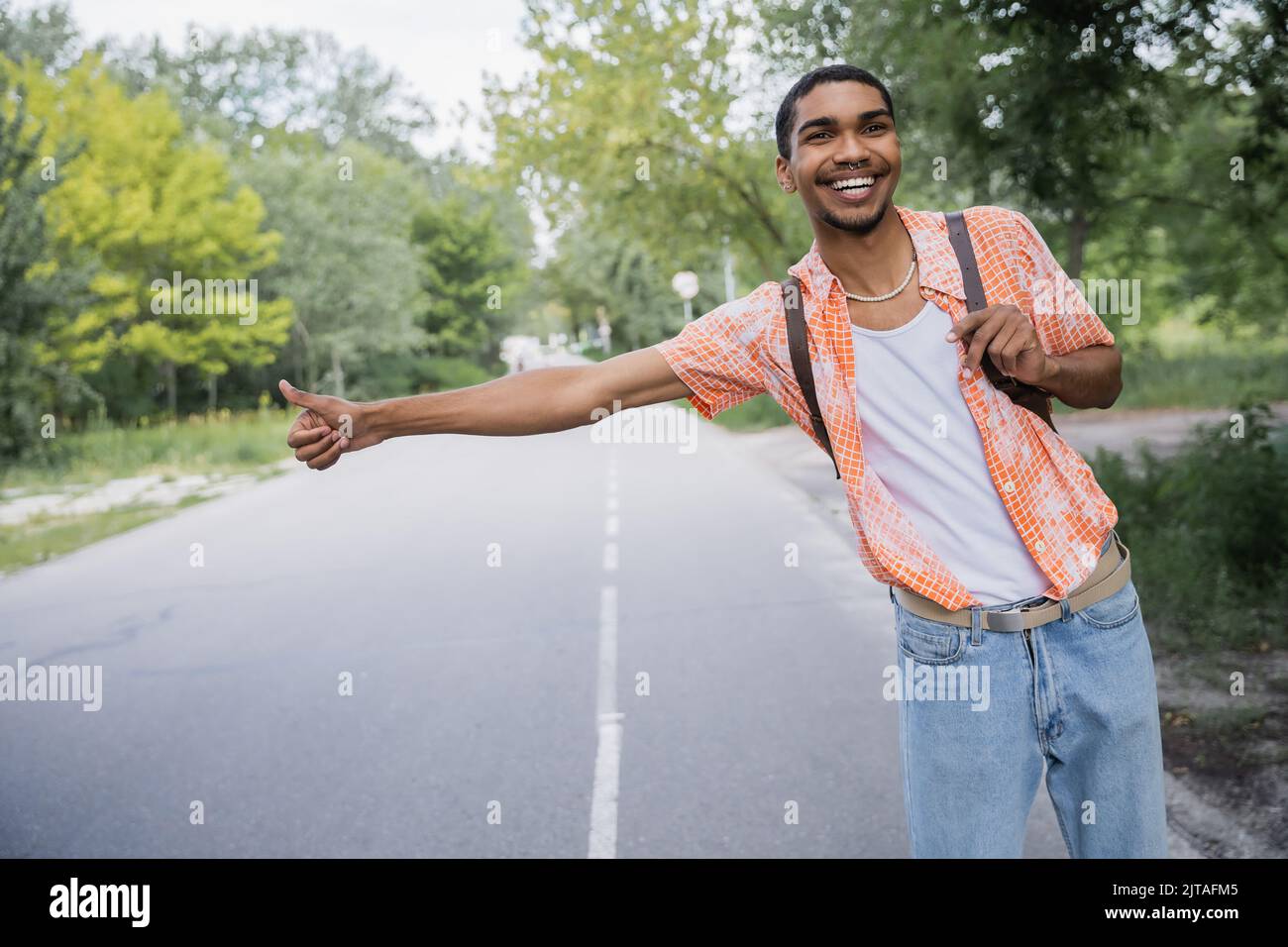 joyful african american hitchhiker with thumb up stopping car on road ...