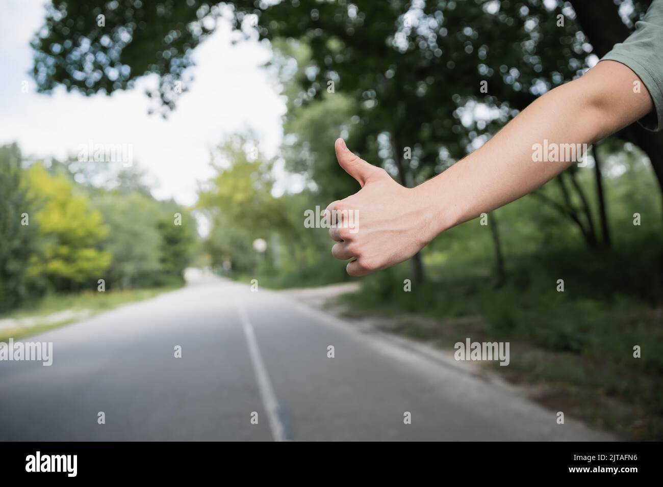 cropped view of hitchhiker with thumb up stopping car on blurred road ...