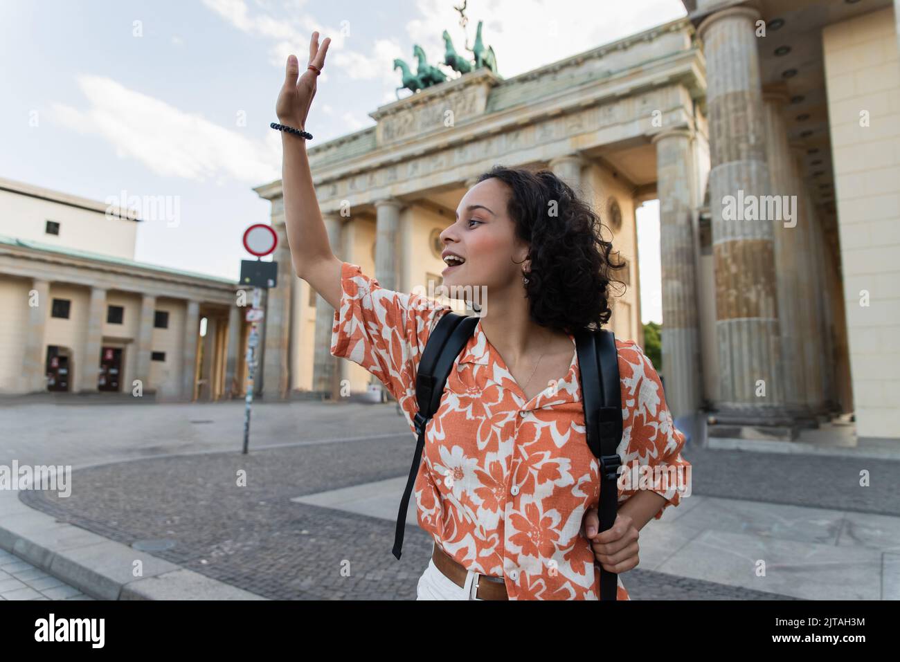 excited tourist with backpack waving hand near brandenburg gate in ...