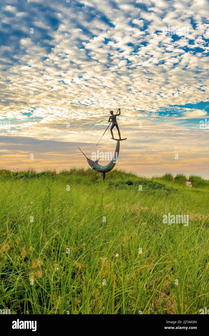 A sculpture of a swordfish harpooner near a beach at sunset in the ...