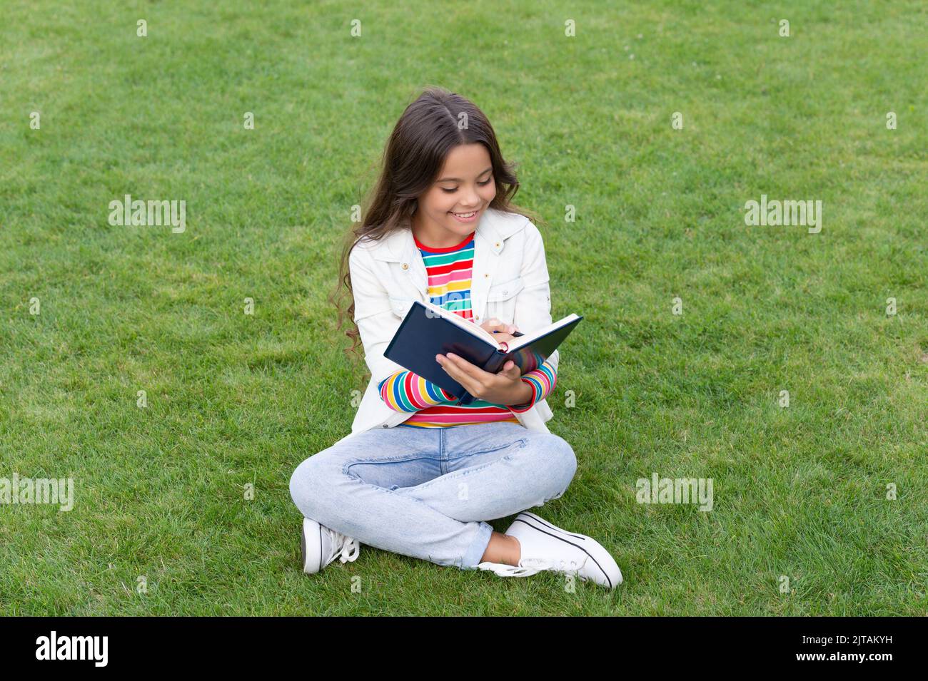 happy teen girl making notes in notebook sitting on grass. taking notes ...