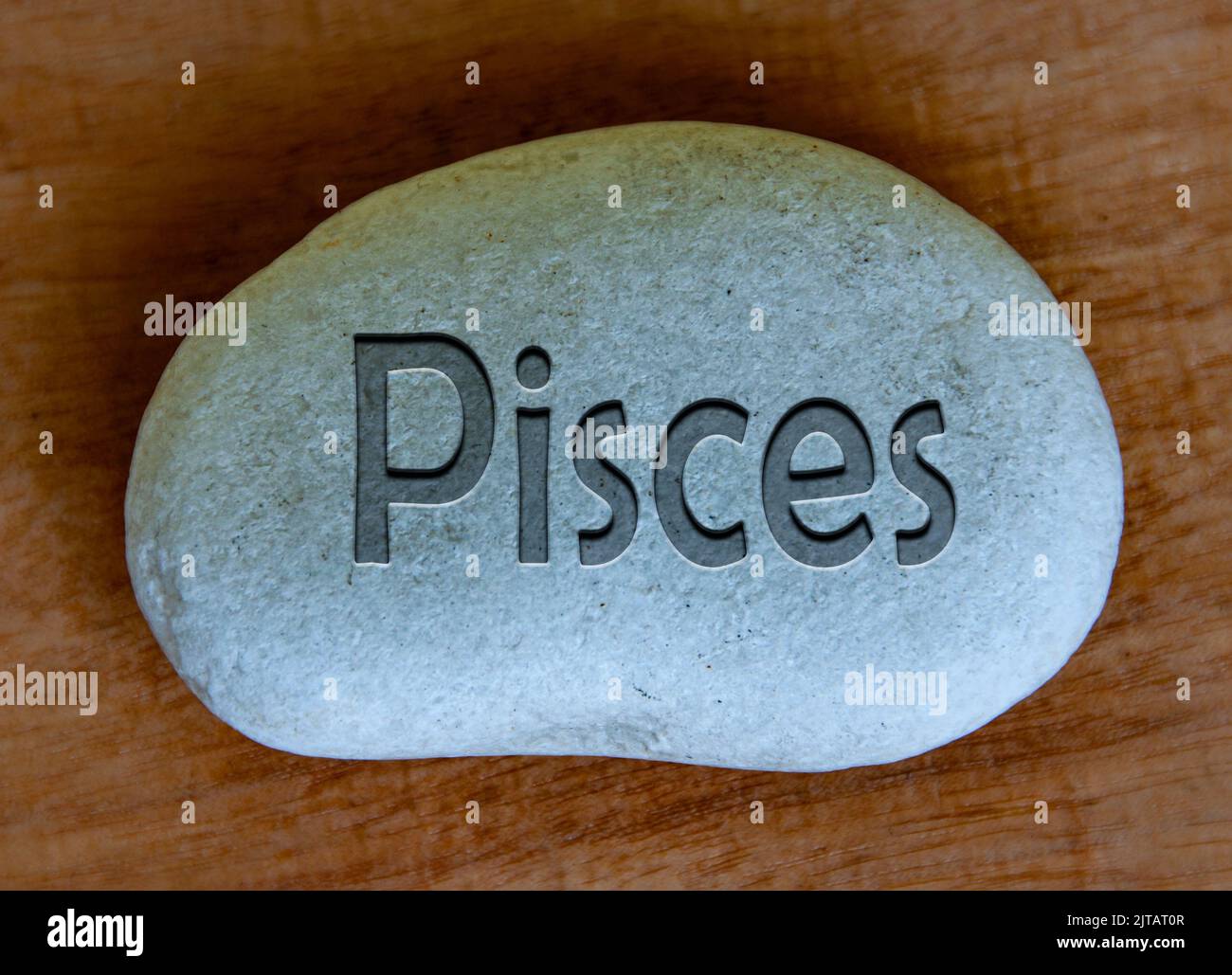 Pisces zodiac sign text engraved on a stock with wooden background ...