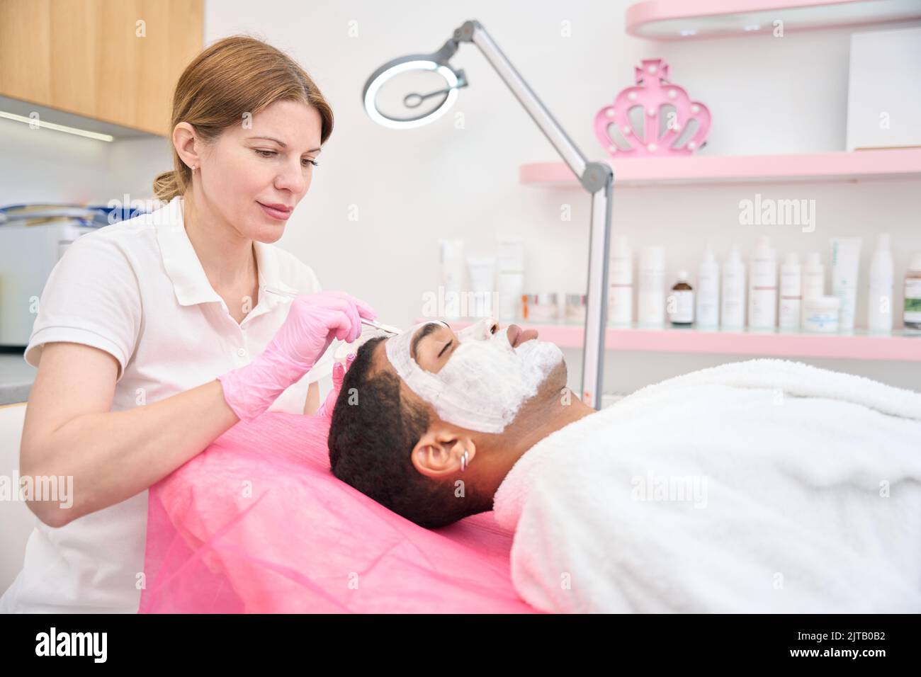 Experienced aesthetician applying mask to facial skin of young man ...