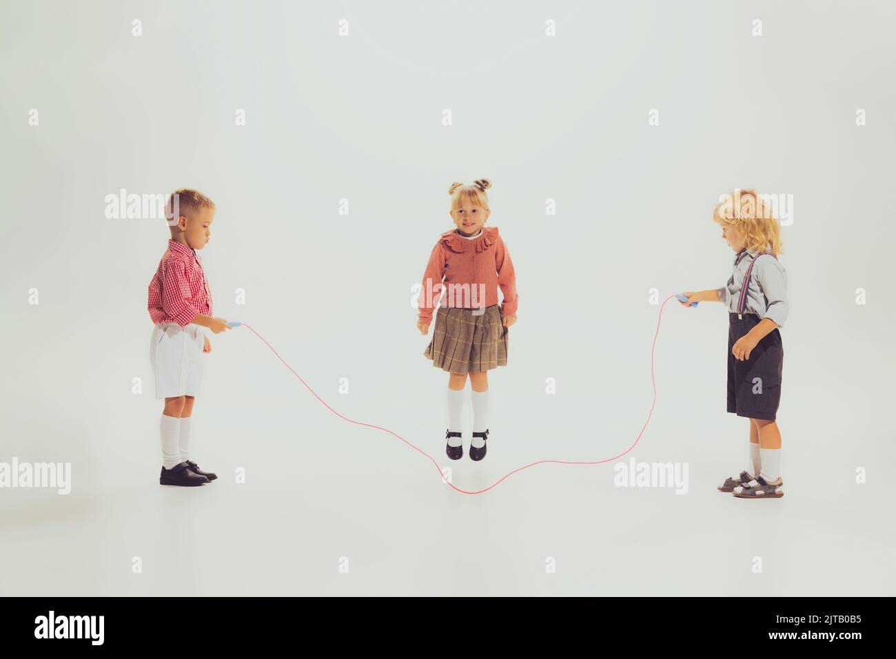 Portrait of children, boys and girl playing together, jumping over rope ...