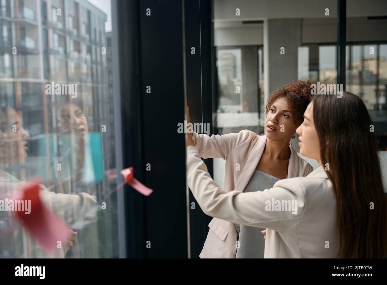 Joyful female co-workers sticking stickers to window with work tasks ...