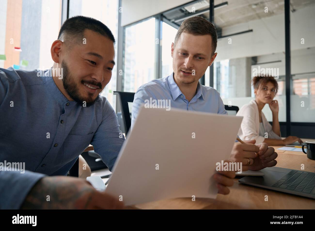 Male colleagues reviewing documents together while sitting in open ...