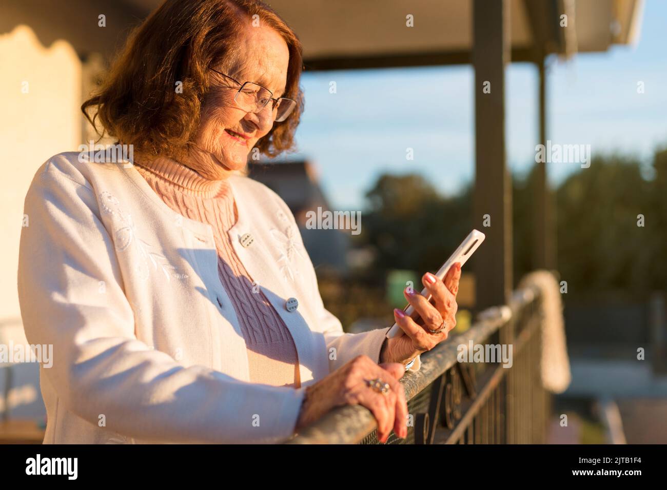 Smiling elder caucasian woman using a smart phone on the balcony of her ...