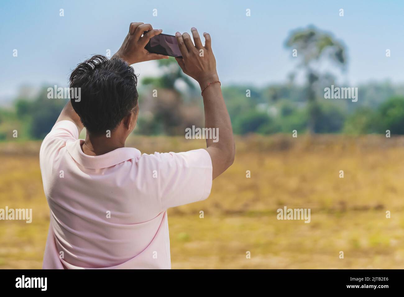 Back view of Asian man using cell phone to take sky photo in field ...