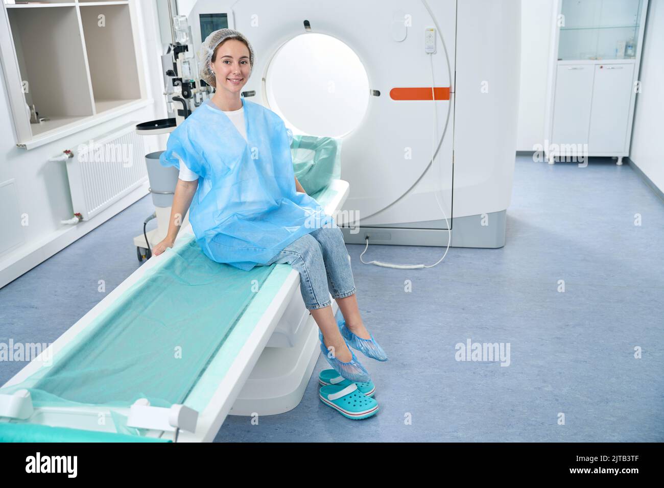 Woman smiling while sitting on CT scanner Stock Photo - Alamy