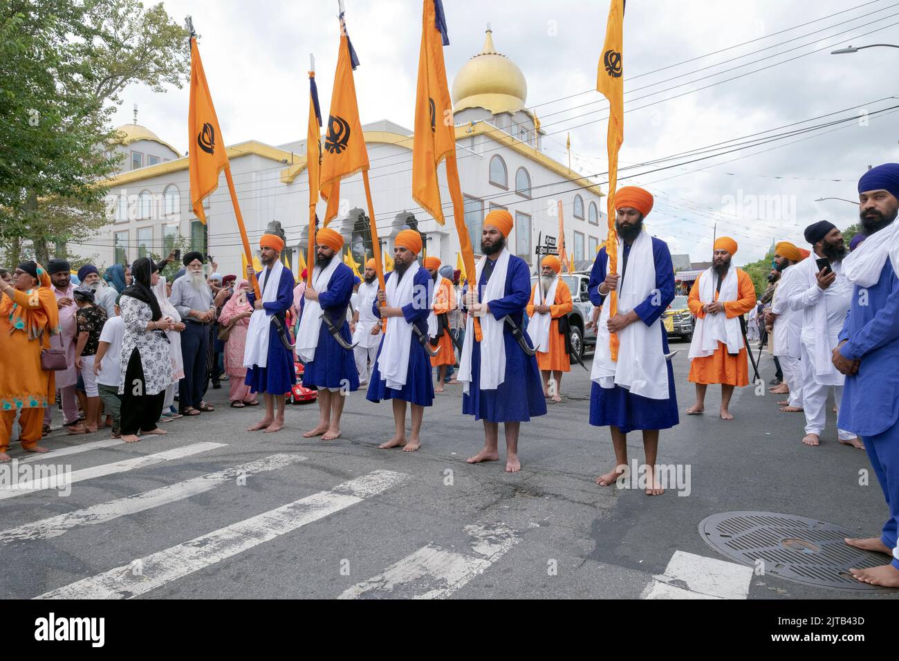 5 Sikh men in blue robes & orange turbans hold flags outside the Sikh ...