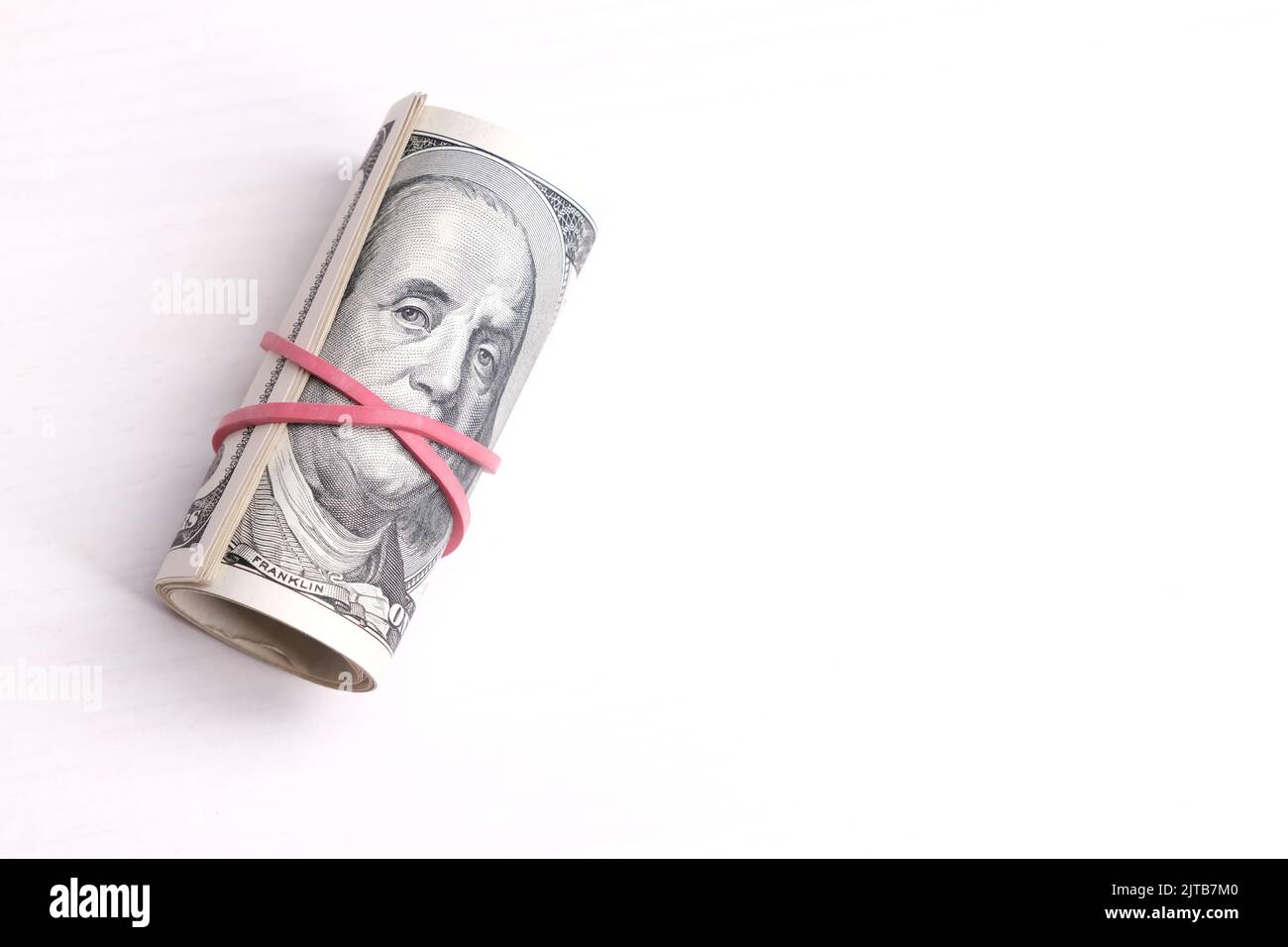 100 dollar bills are rolled up and tied with a rubber band. white ...