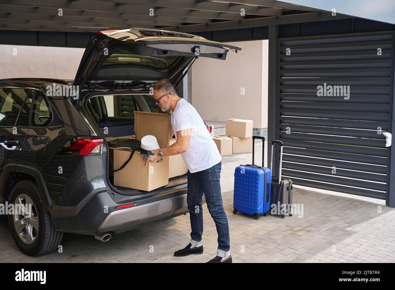 Adult man puts boxes of things in trunk of car Stock Photo - Alamy