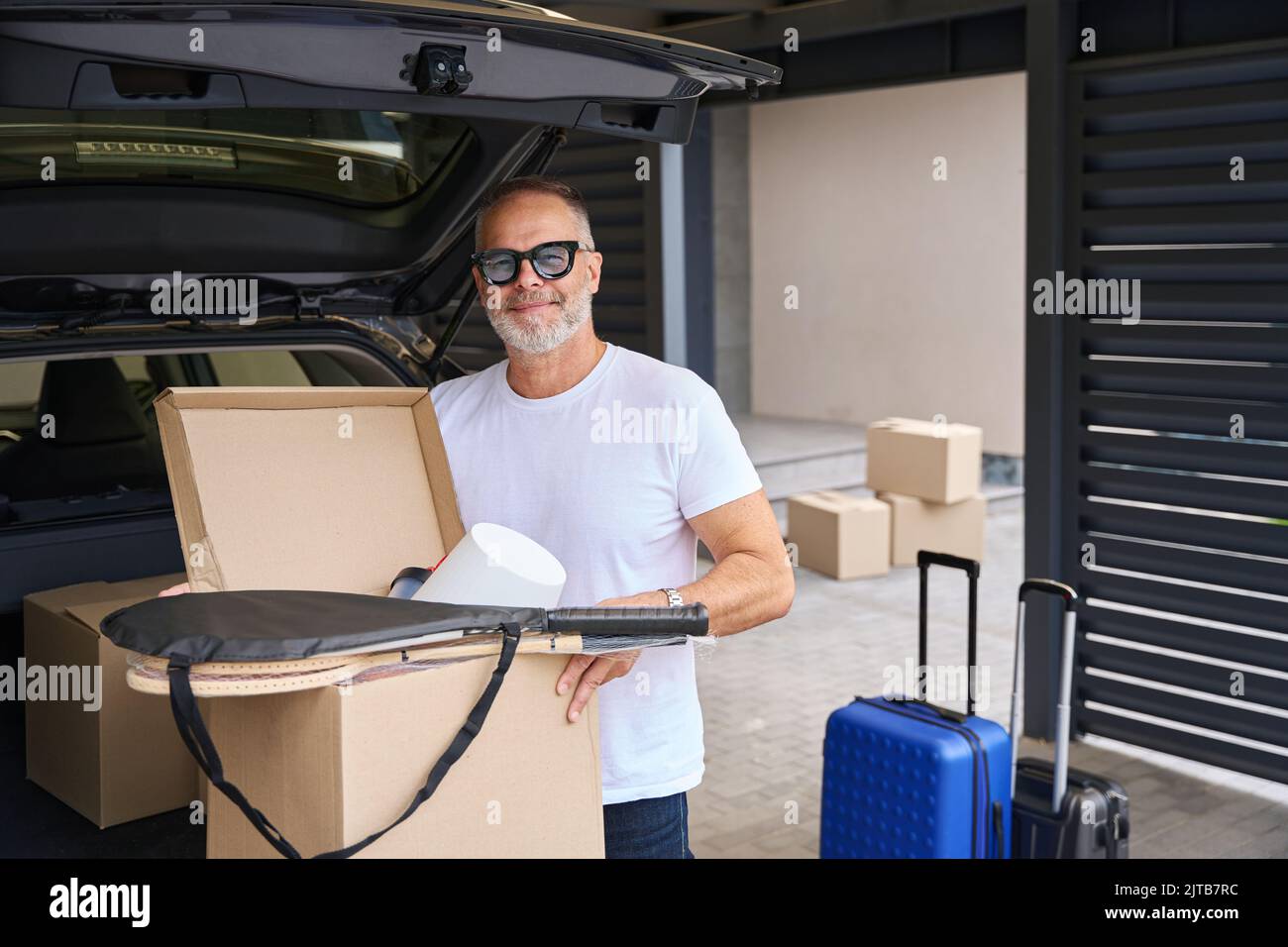 Man holding boxes while standing near open car trunk Stock Photo - Alamy