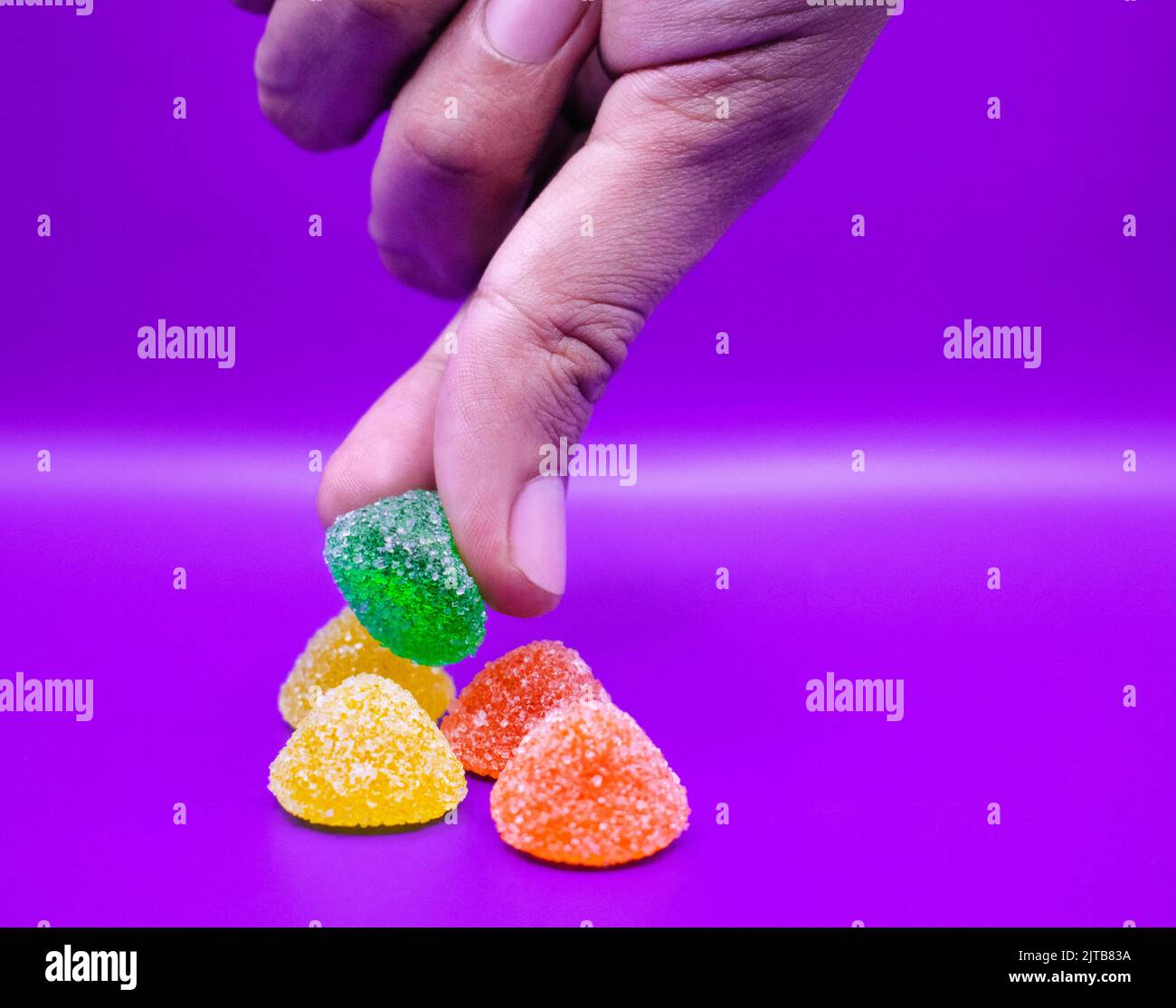 A hand holding candy gums on a purple background Stock Photo - Alamy