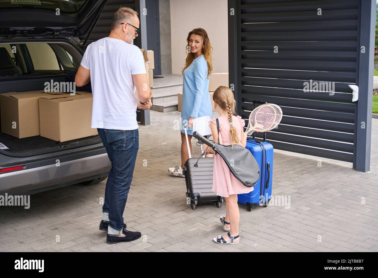 Joyful father, mother, daughter carry things from car to house Stock ...