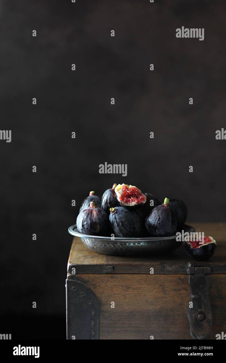 Black fresh figs in a metalic plate on dark background. Copy space ...