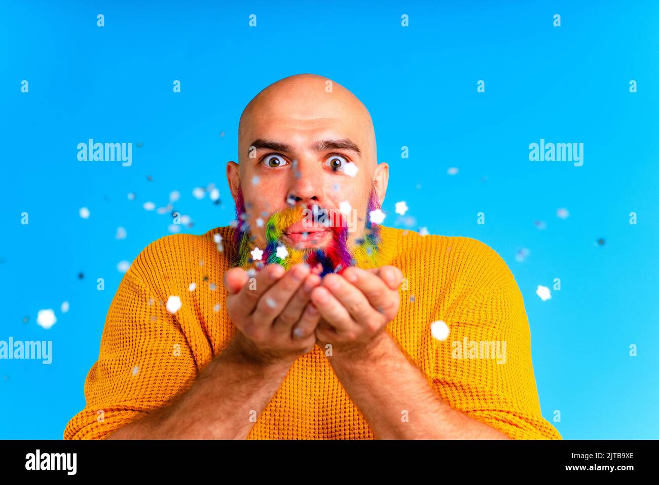 handsome man with raindow in beard and yellow sweater blowing glitter ...