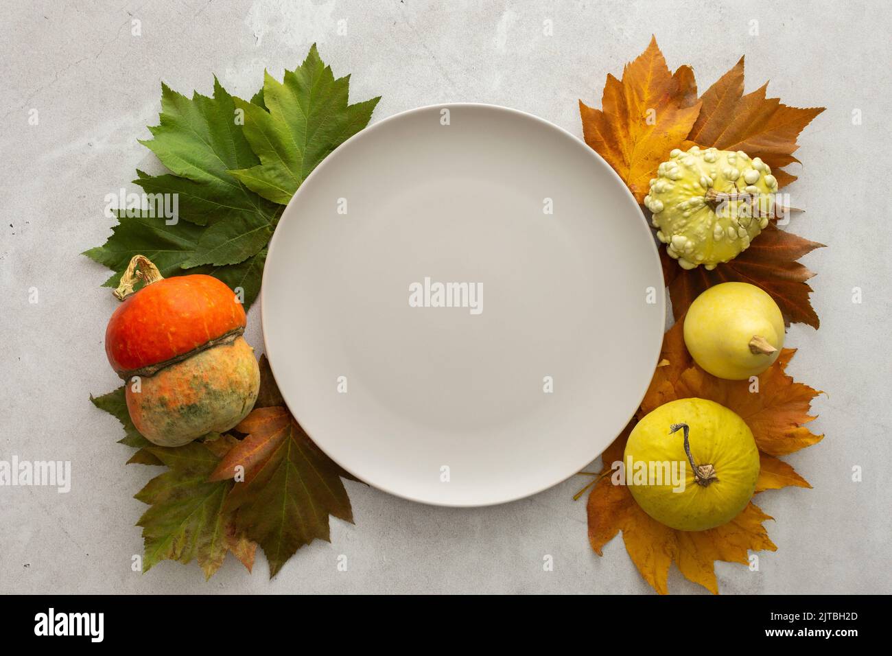 Autumn table setting, fallen maple leaves and pumpkins next to a plate ...