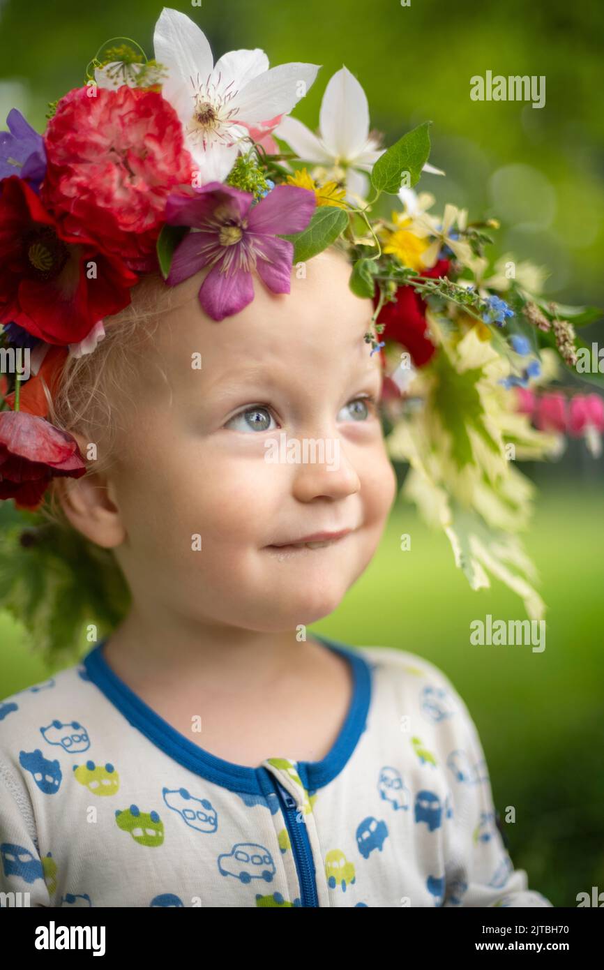 A young boy wears a flower crown with red poppies, blue campanula, and ...