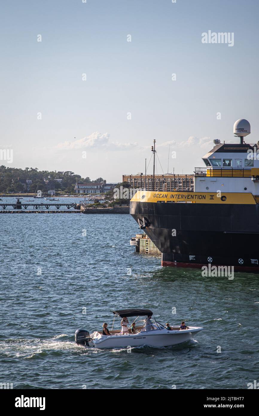 A small white boat passing by an ocean research ship in the Woods Hole ...