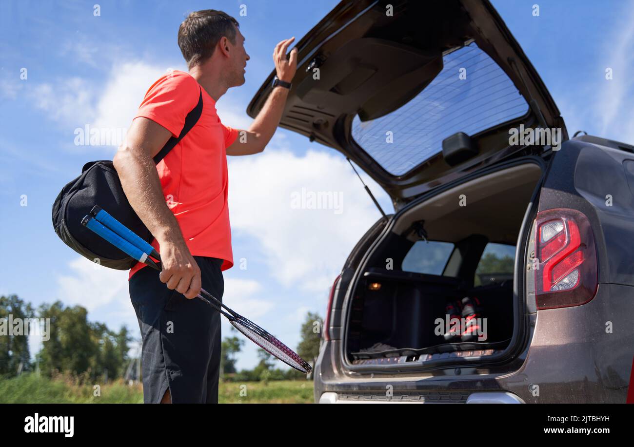 Sportsman getting bag and badminton rackets out of trunk outdoors ...
