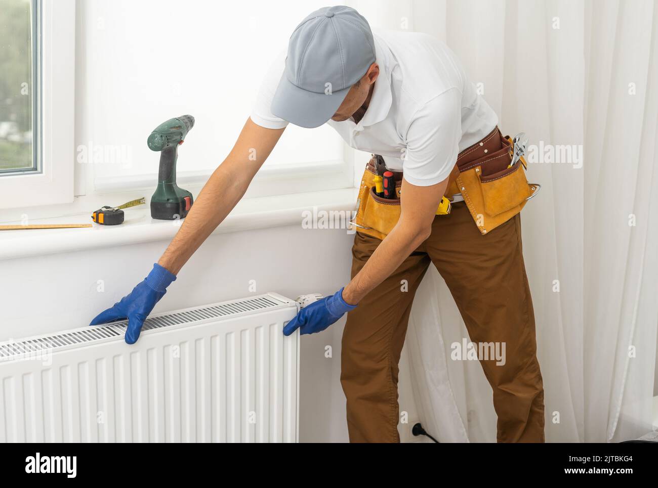 A male plumber installs a radiator in the heating system of an ...