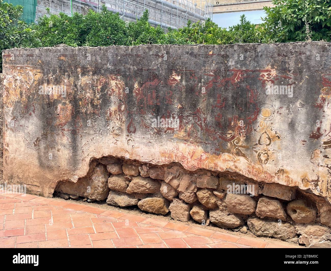 A partly destroyed wall with faded red paint patterns. Bricks showing ...