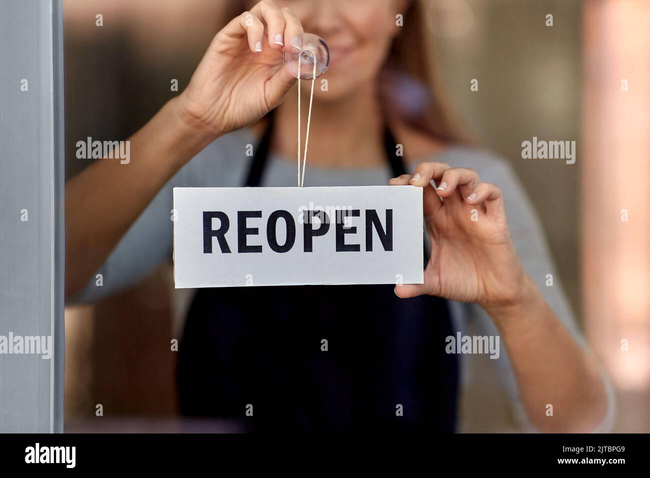 happy woman hanging reopen banner on door glass Stock Photo - Alamy