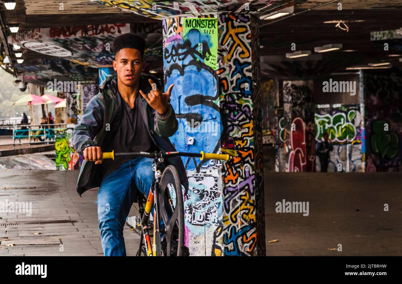 A black youth riding his bike on one wheel makes gesture with his ...