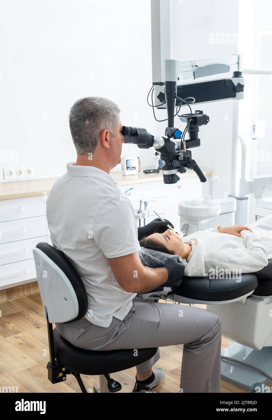 Dentist using dental microscope treating patient teeth at dental clinic ...