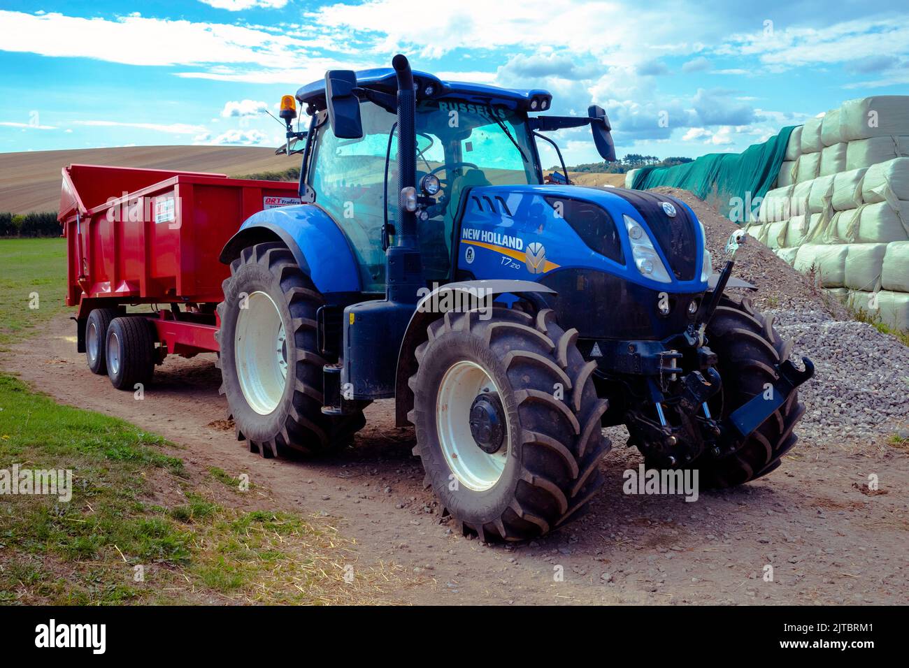 A blue New Holland T7 farm tractor and a tipping trailer at a farm in ...