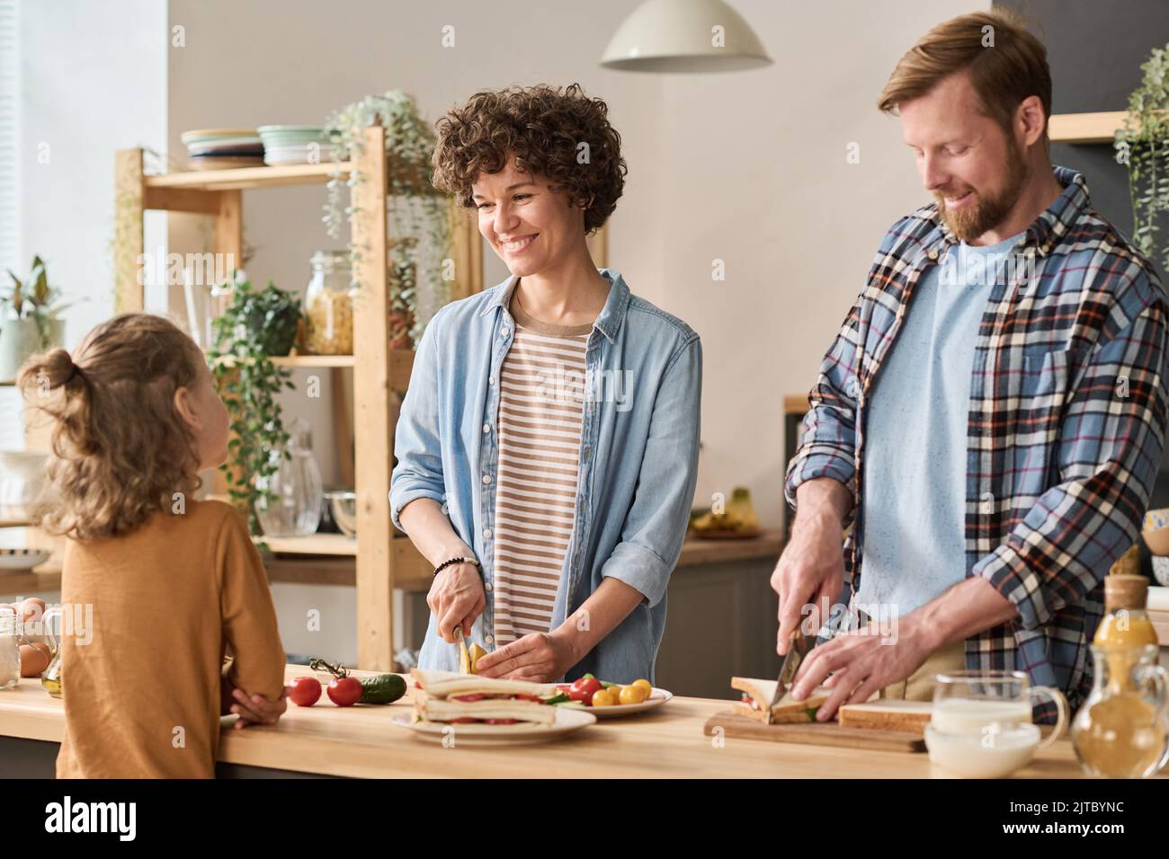 Happy family preparing sandwiches at table in kitchen and talking to ...