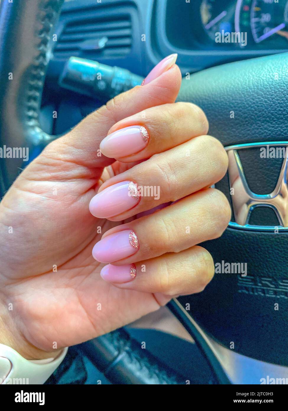 female hands demonstrating fresh manicure hold the steering wheel of a ...